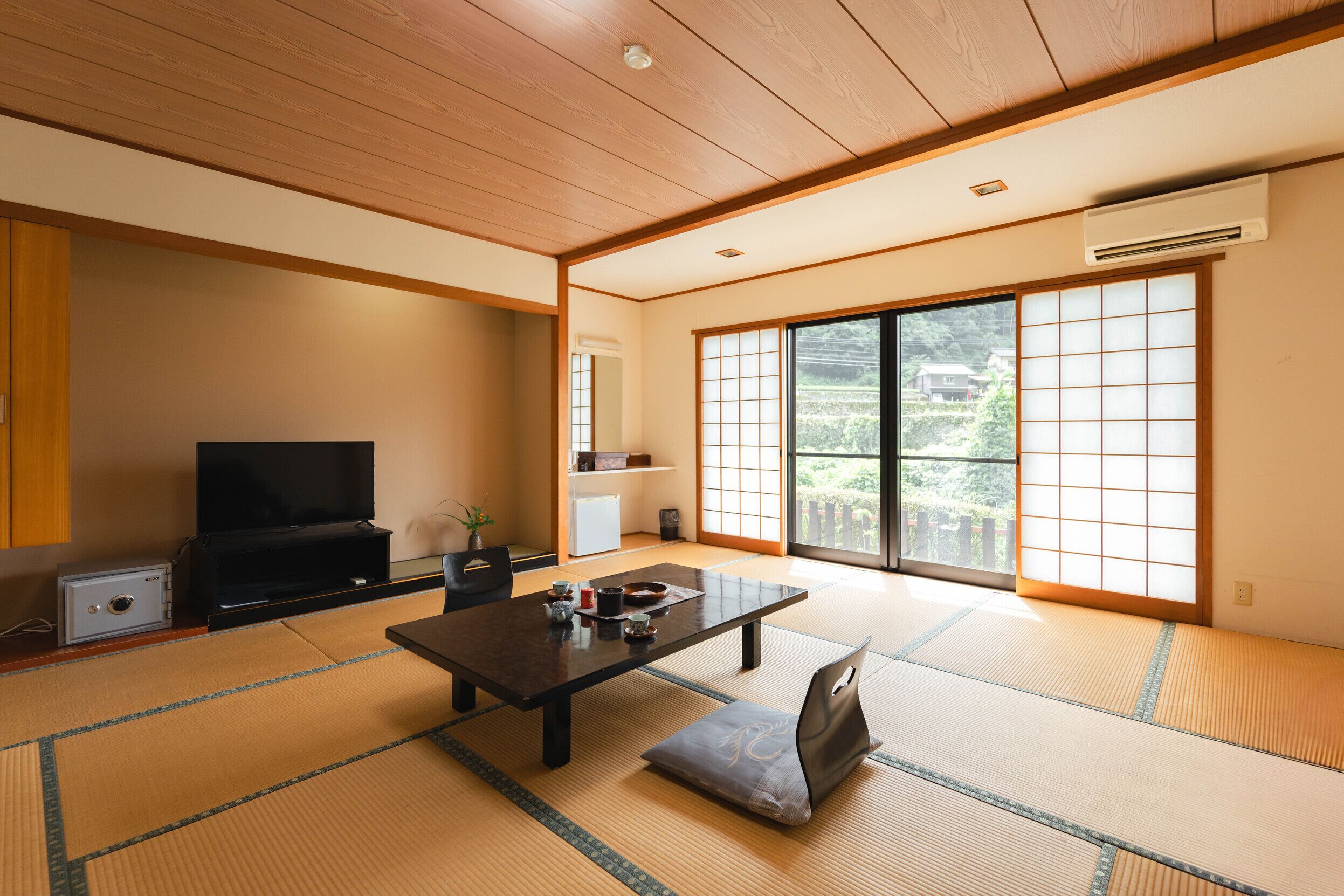 Um quarto japonês tradicional com tatames, televisão, um pequeno armário e uma porta deslizante para uma varanda.