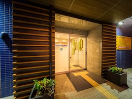 Entrada de hotel com design moderno, incluindo porta de vidro, rampa para acessibilidade e uma placa.