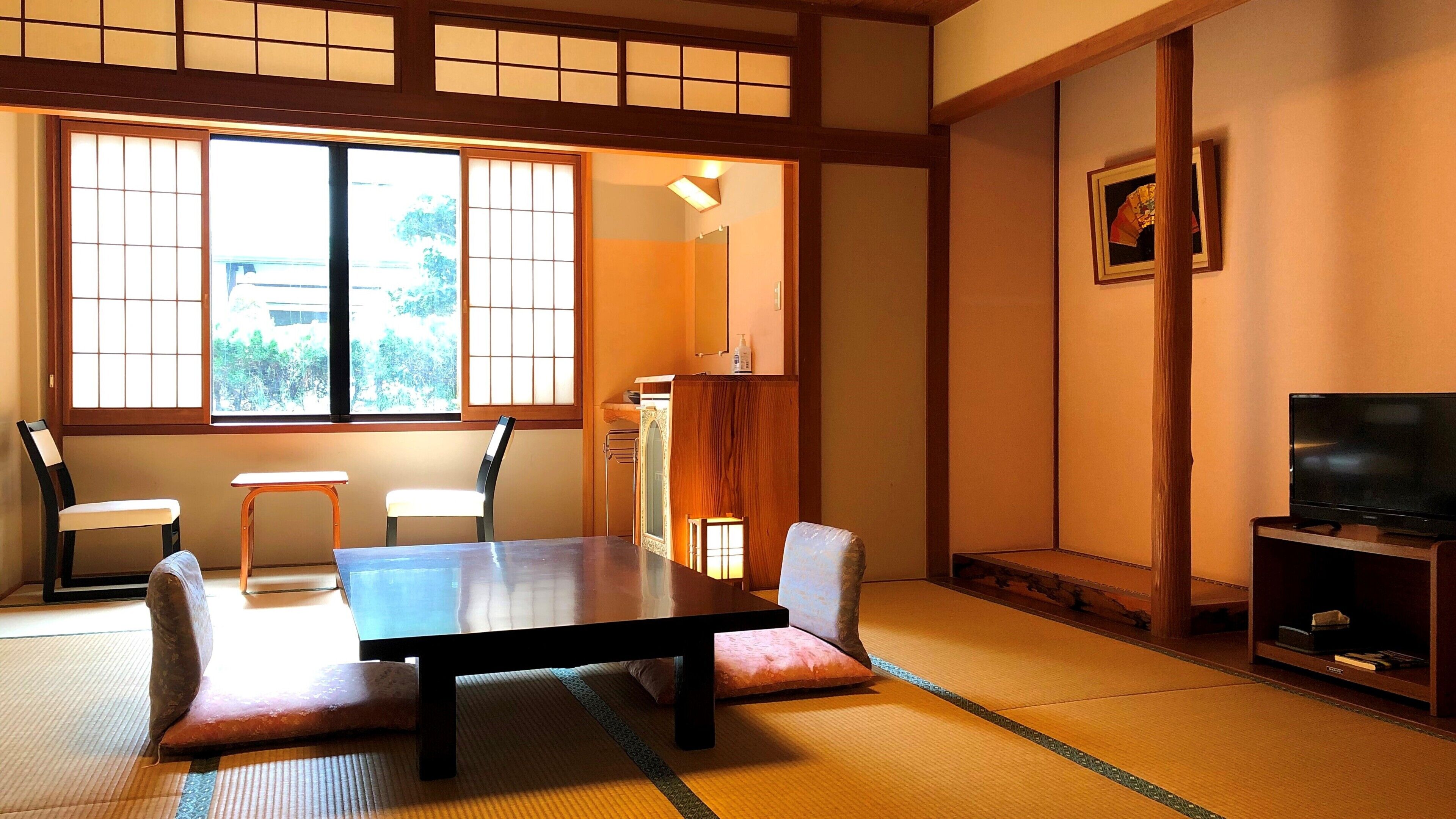 Um quarto japonês tradicional com tatames, uma mesa baixa e uma televisão.