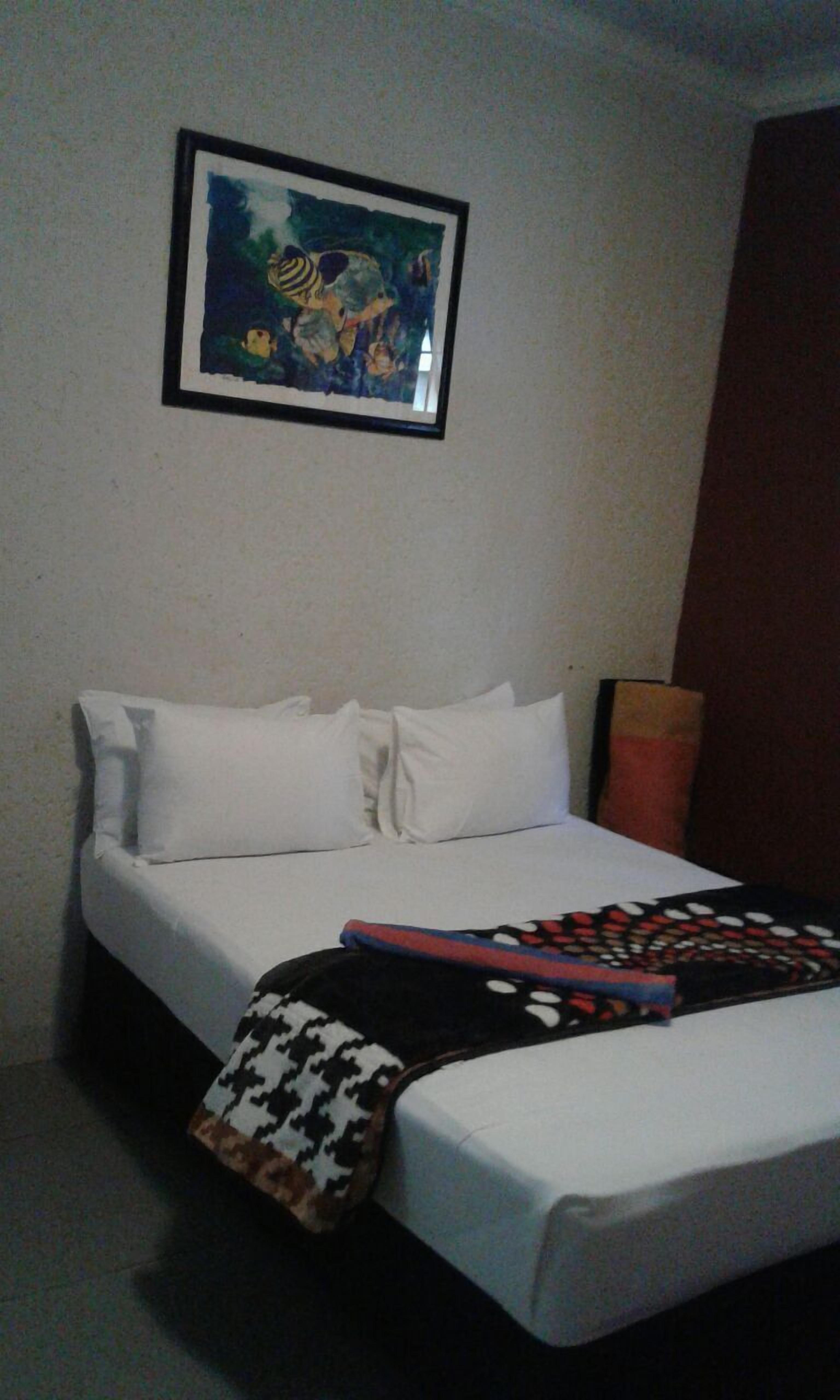 Quarto com cama, roupa de cama branca, quadro na parede e manta decorativa.