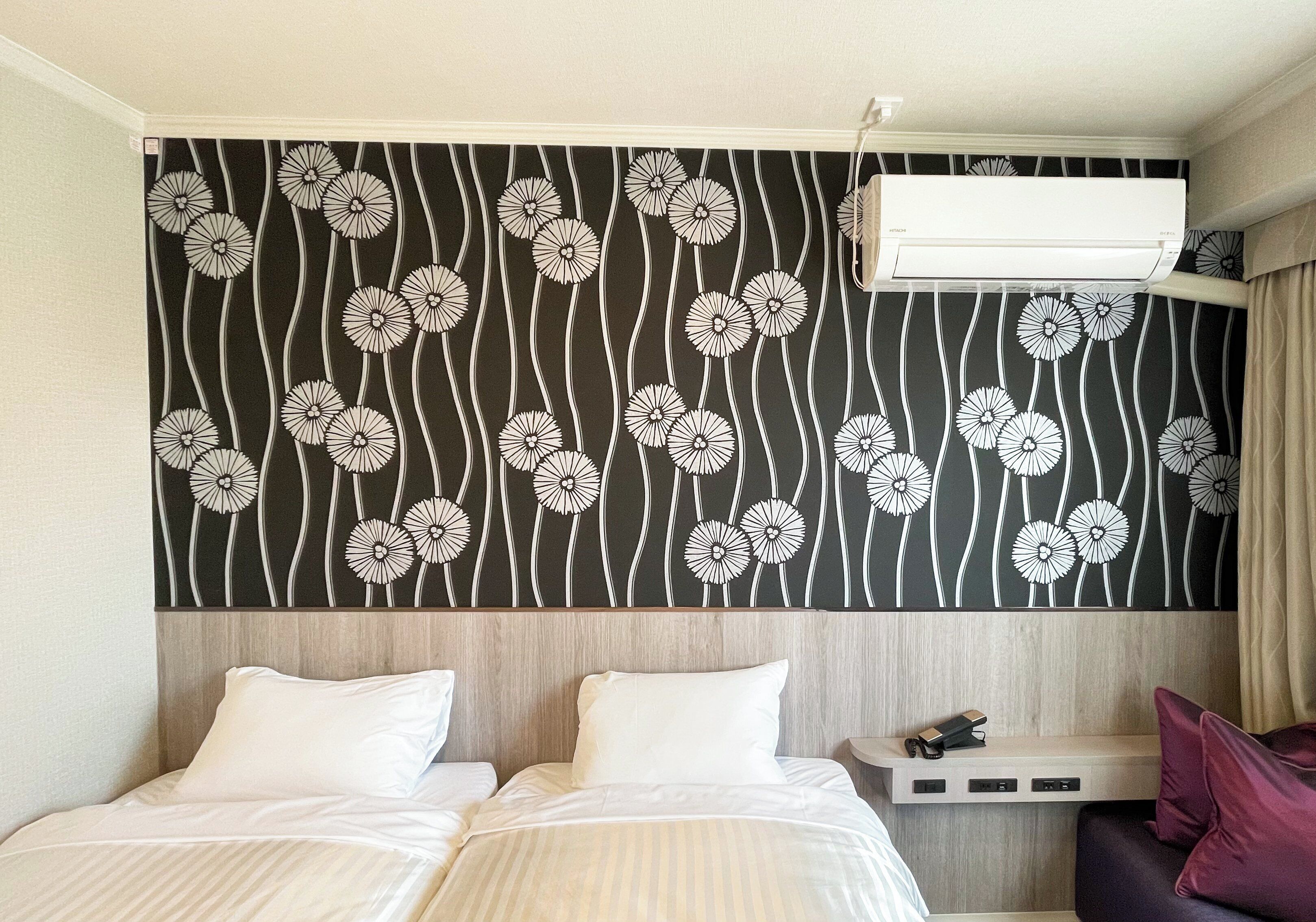 Quarto de hotel com cama, mesas de cabeceira, sofá e parede com padrão floral.
