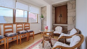 Uma sala de estar com cadeiras de madeira, uma mesa de vidro e uma parede de pedra.