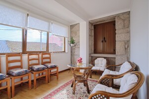 Uma sala de estar com cadeiras de madeira, uma mesa de vidro e uma parede de pedra.