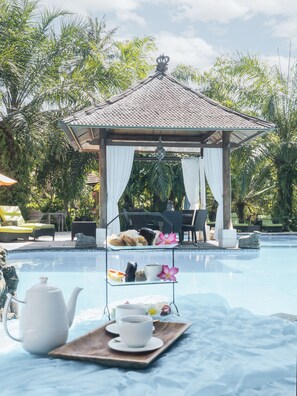 Área de piscina com um gazebo, cadeiras de descanso e uma bandeja com doces e um bule de chá.