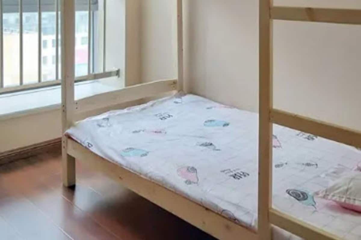 Uma cama beliche com colchão decorado com personagens de desenho animado, uma janela com vista para edifícios e um respiradouro no teto.