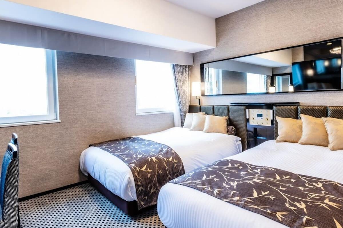 Quarto de hotel com duas camas, um espelho grande, uma TV de tela plana e um painel de controle.