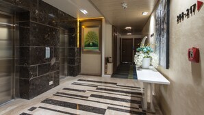Um hall de hotel com piso de mármore, um balcão de recepção, um telefone fixado na parede e uma câmera de segurança.