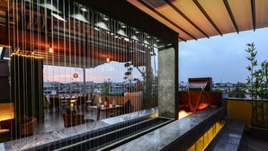 Um bar no terraço com vista para o horizonte urbano, mesas ao ar livre e uma lareira.