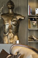Uma estátua de bronze de uma figura humana com a etiqueta "MELIA" em frente a uma estante de livros e uma moldura com uma fotografia.