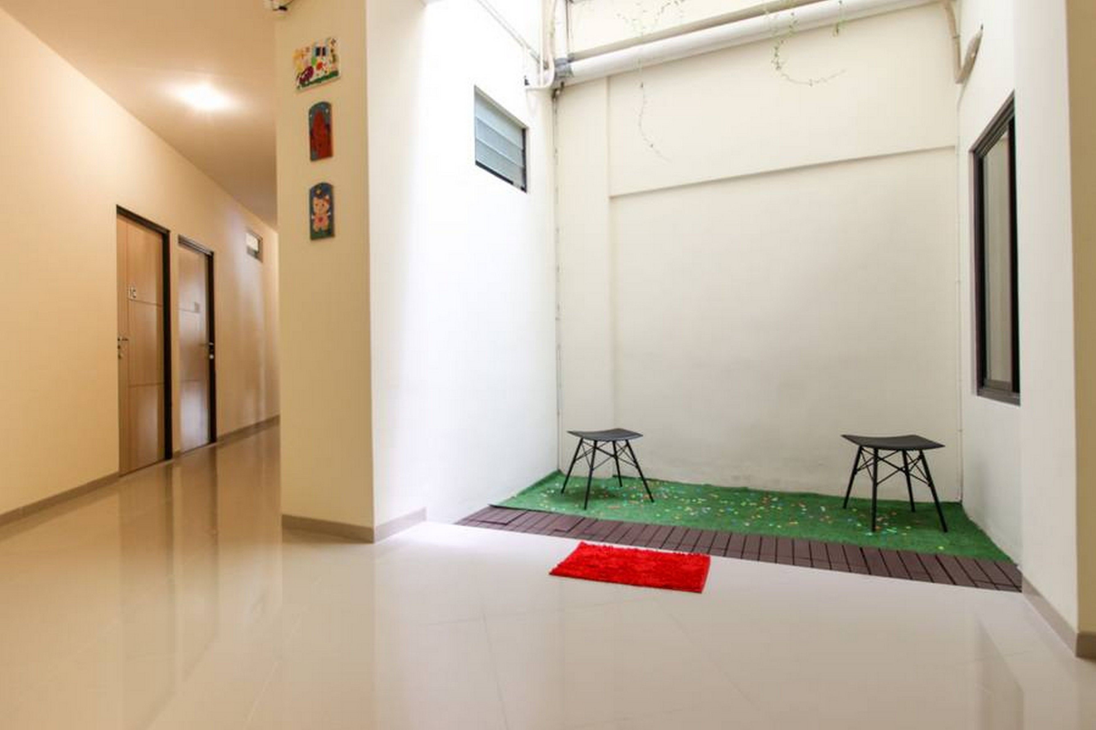 Um corredor com duas portas, um tapete vermelho e uma pequena área externa com uma mesa e uma cadeira.
