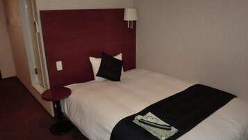 Quarto de hotel com uma cama grande, uma mesa de cabeceira redonda, cabeceira vermelha e uma luminária fixada na parede.