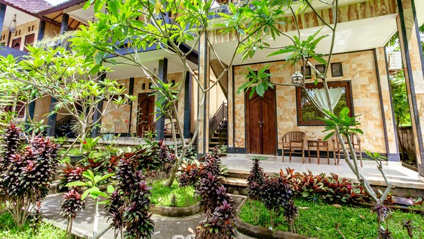 Um edifício de dois andares com área de estar coberta, escadas e um jardim com diversas plantas.