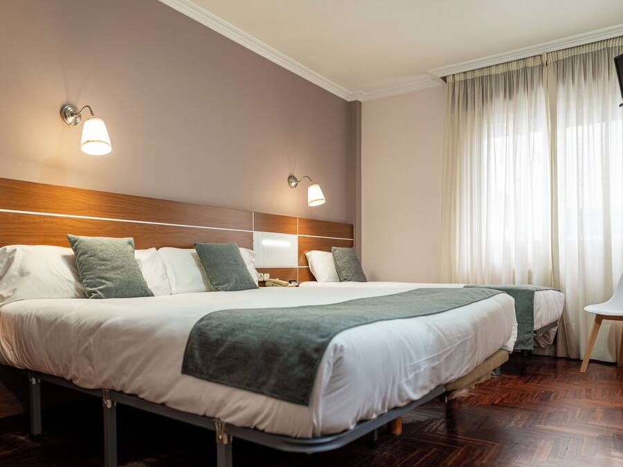 Quarto de hotel com duas camas, televisão, cadeira e janela com cortinas.