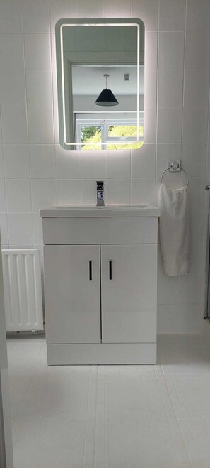 Casa de banho com toucador branco, espelho com moldura preta e porta-toalhas.