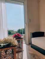 Quarto com cama, uma mesa com flores e vista para o verde através de uma porta de vidro.