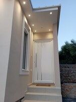 Entrada de um edifício moderno com porta branca, janela e parede de pedra.