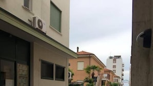 Uma rua estreita com edifícios em ambos os lados, um carro estacionado e uma marcação na via visível.