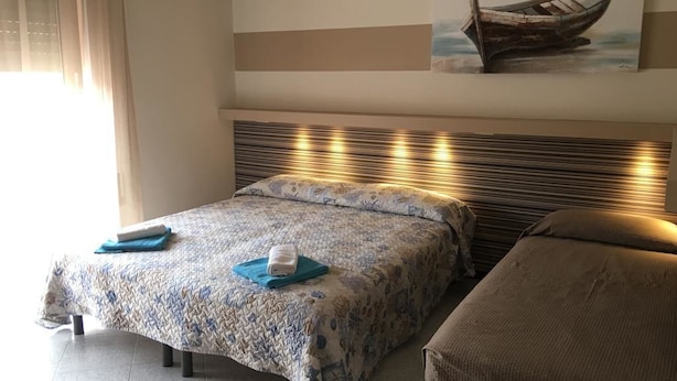 Quarto de hotel com cama, mesa de cabeceira, cabeceira com iluminação, pintura na parede e janela com cortinas.