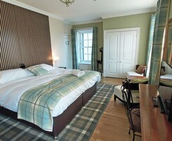 Quarto com cama grande, cabeceira de madeira, escrivaninha com cadeira, janela com cortinas e porta.
