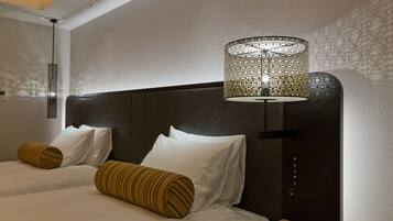 Quarto de hotel com duas camas, cabeceira escura e luminária pendente com padrão geométrico.