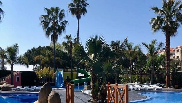 Uma piscina com uma ponte de madeira, espreguiçadeiras e palmeiras.