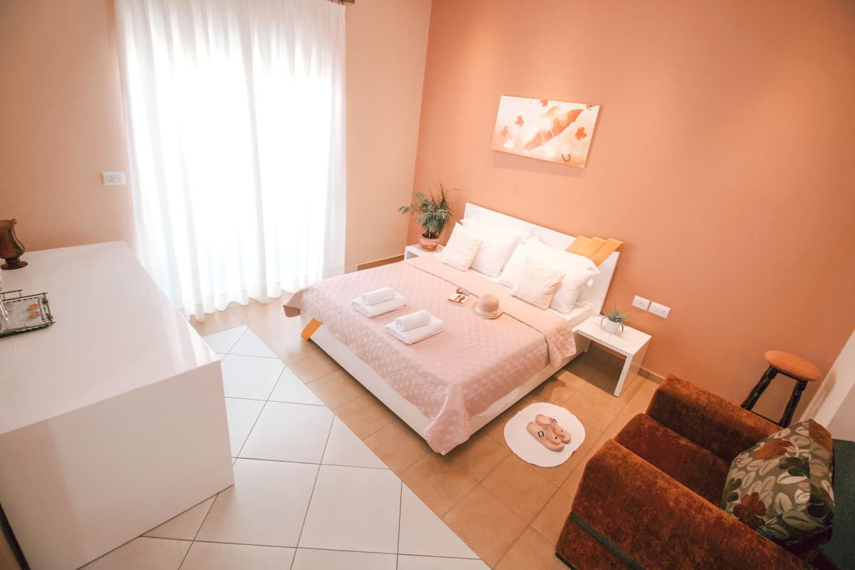 Um quarto com cama, mesas de cabeceira, uma cadeira e uma escrivaninha.