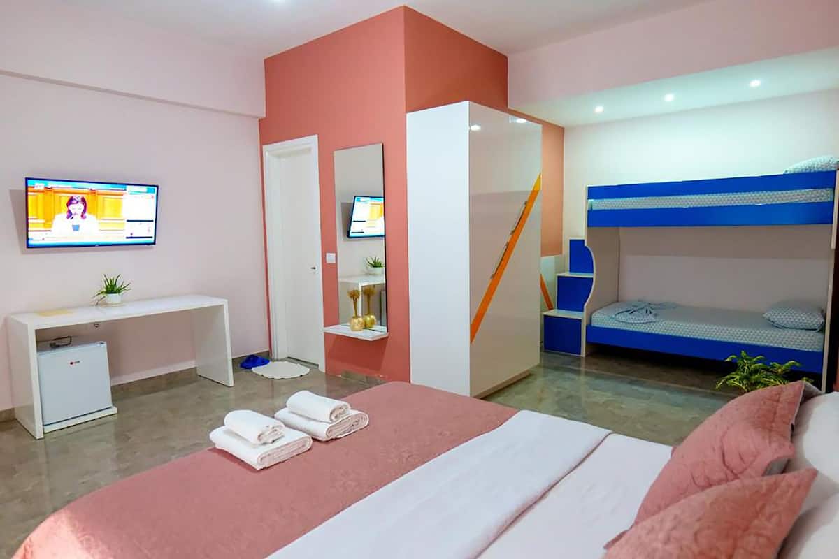 Quarto de hotel moderno com beliche, escrivaninha, TV e mini-geladeira.
