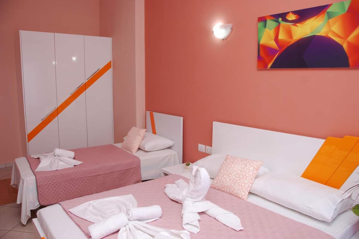 Quarto de hotel com duas camas, um guarda-roupa, um quadro e uma luminária na parede.