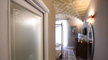 Um corredor com piso estampado, porta com vidro decorativo, espelho e quadro na parede.