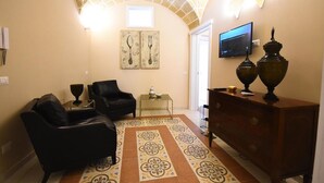 Uma sala de estar com um tapete estampado, um sofá, uma mesa de centro, uma televisão e vasos decorativos.