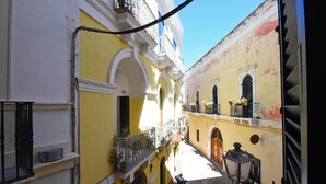 Uma rua estreita com edifícios amarelos, um carrinho pequeno e uma pessoa sentada num banco.