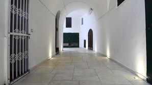 Um corredor com paredes brancas, chão de azulejos e um portão de metal à esquerda.