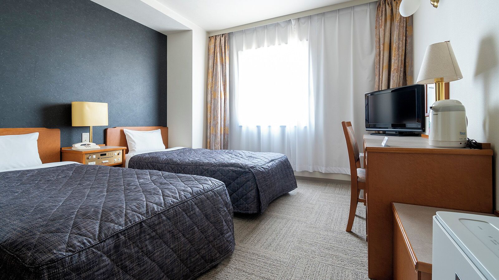 Quarto de hotel com duas camas, uma escrivaninha, televisão, abajur e cafeteira.
