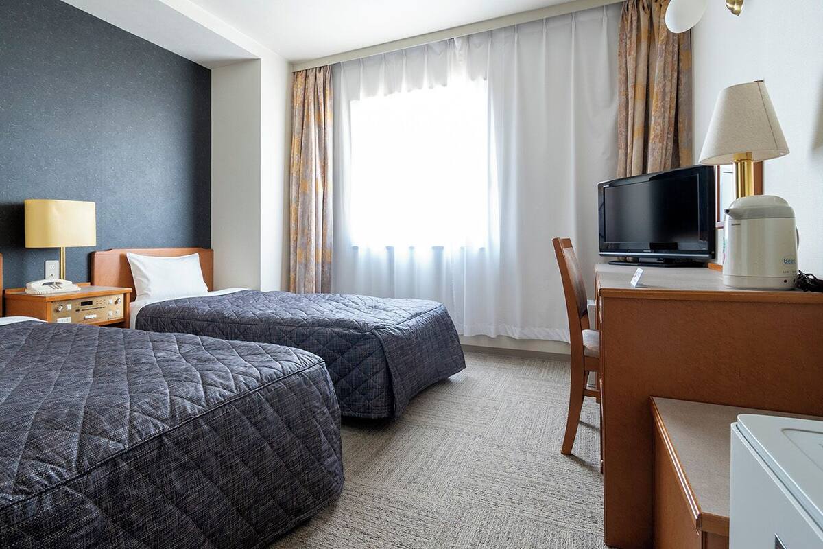 Quarto de hotel com duas camas, uma escrivaninha, televisão, abajur e cafeteira.
