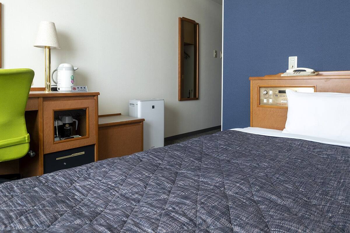 Quarto de hotel com cama, escrivaninha com luminária, cafeteira e espelho.