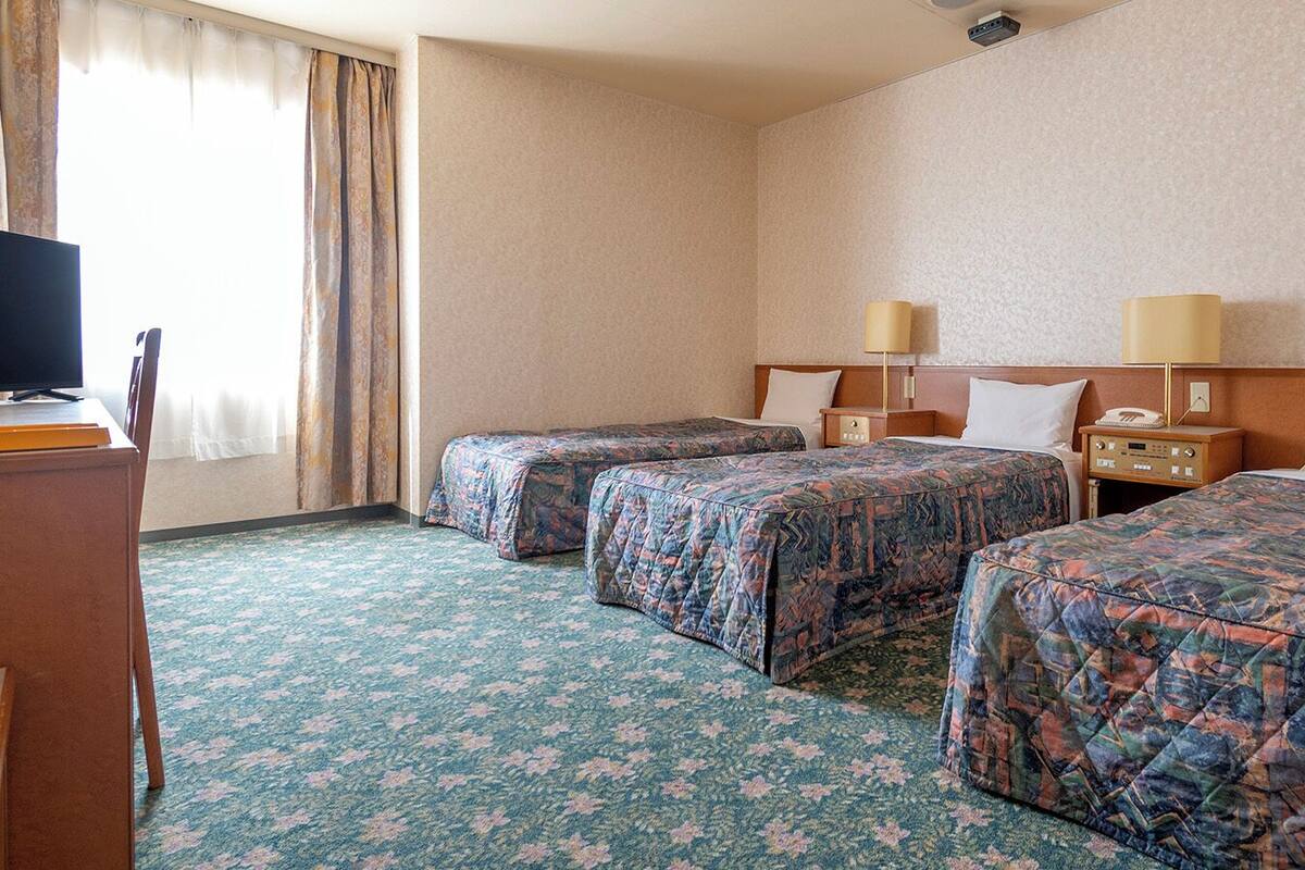 Quarto de hotel com três camas, uma escrivaninha e uma televisão.