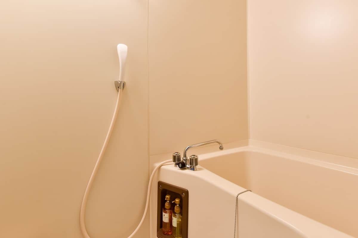 Um banheiro com banheira, chuveiro e dois frascos de shampoo.