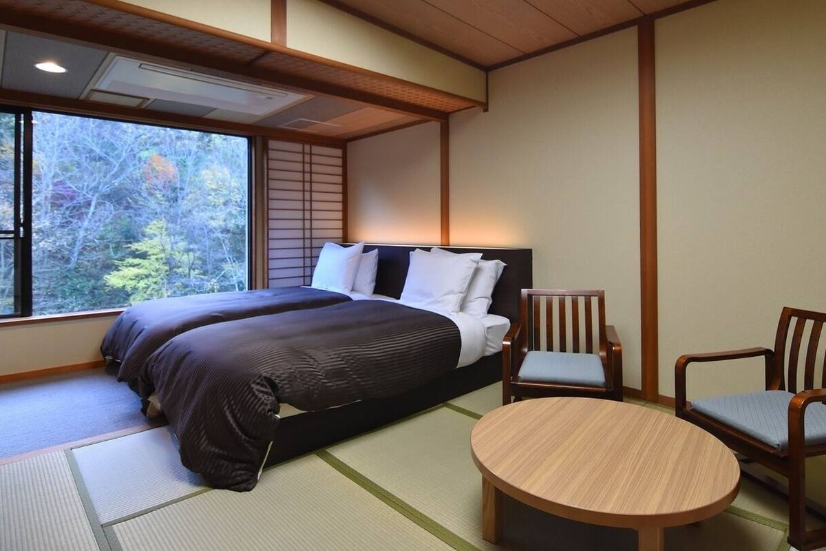 Quarto com uma cama, duas cadeiras, uma mesa redonda e uma janela grande.
