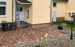Um edifício com um pátio pavimentado, uma mesa pequena com cadeiras e um poste de luz.