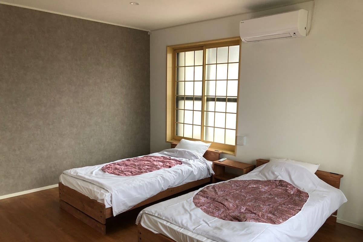 Quarto com duas camas de madeira, janela com persianas e ar condicionado na parede.