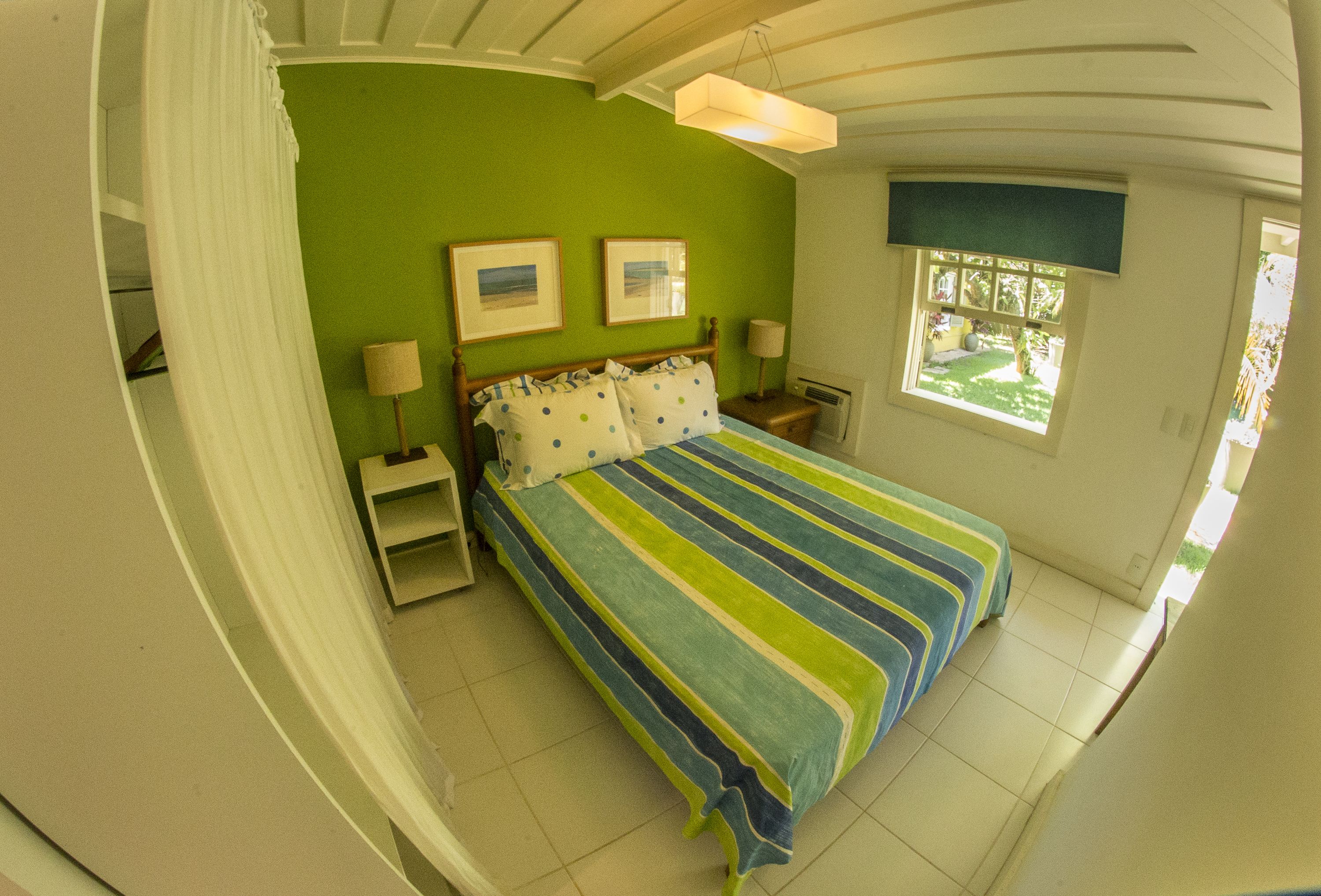 Quarto com uma cama, duas mesas de cabeceira, uma janela e uma parede verde.