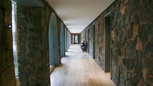Um corredor longo com paredes de pedra e soalho de madeira, que dá para um quarto com uma janela grande.