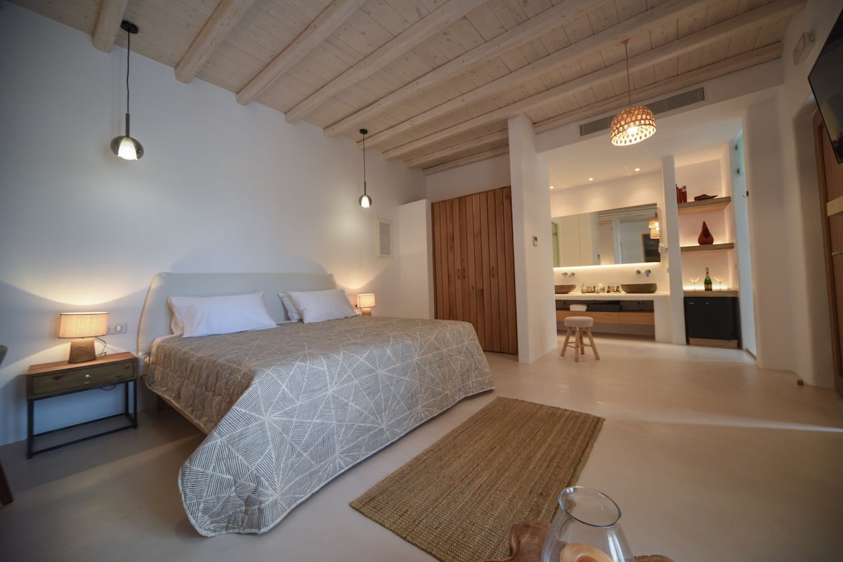 Quarto com cama grande, mesas de cabeceira, guarda-roupa de madeira e vista para a cozinha.