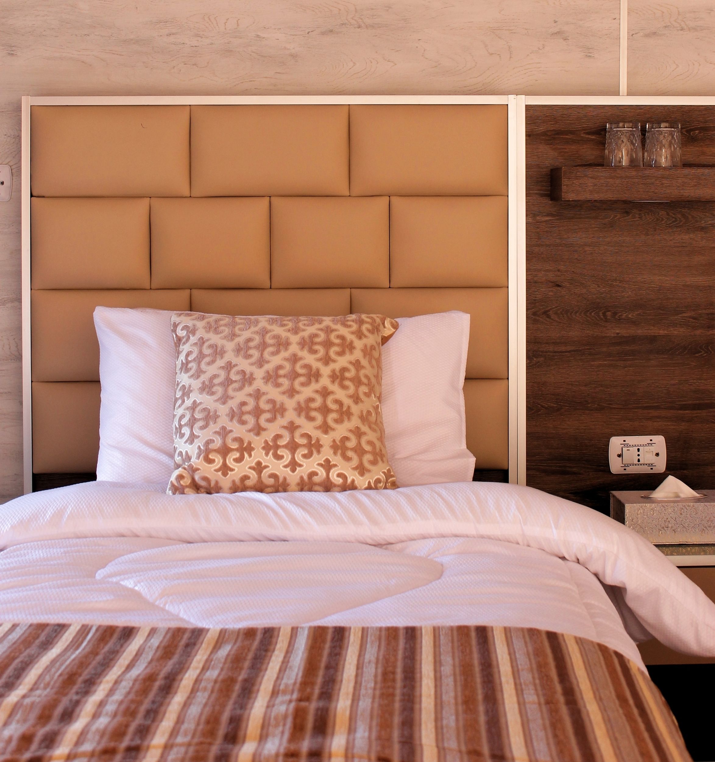 Cama bem arrumada com manta listrada, almofada estampada e cabeceira de madeira.