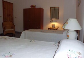 Quarto com duas camas, um guarda-roupa de madeira, uma cadeira, uma mesa com abajur e um espelho na parede.