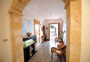 Um corredor com arcos de pedra, um aquário, cadeiras de vime e um mapa na parede.