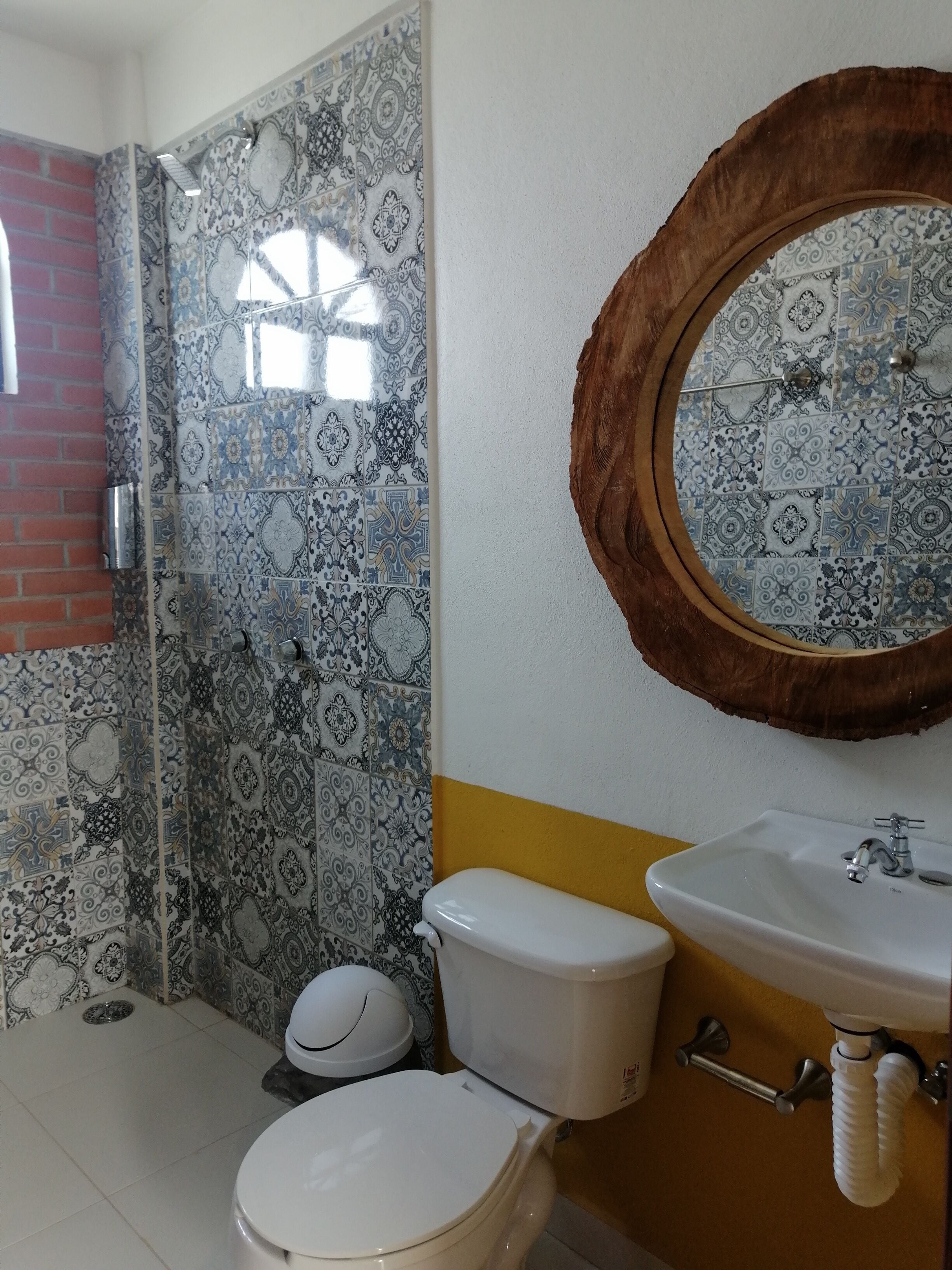 Casa de banho com azulejos estampados, sanita, lavatório e espelho com moldura de madeira.