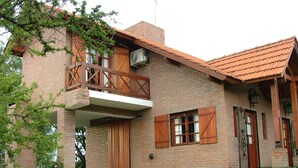 Uma casa de dois andares em tijolo, com varanda, porta principal e pequeno alpendre.