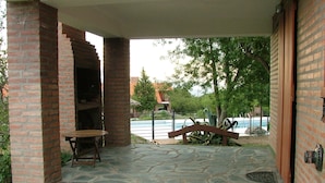 Uma área de varanda coberta com piso de pedra, parede de tijolos e vista para uma piscina.
