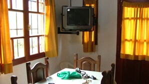 Uma sala de jantar com uma mesa, cadeiras, uma televisão na parede e cortinas nas janelas.